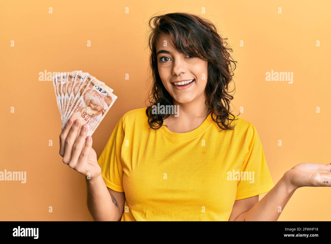Une jeune femme hispanique détient 50 billets de lira turcs célébrant son succès sourire heureux ...