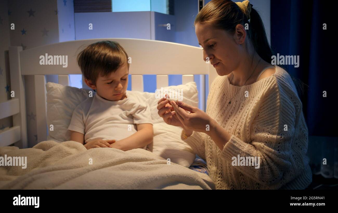 Jeune mère qui s'occupe de mesurer la température et embrasse son petit ...