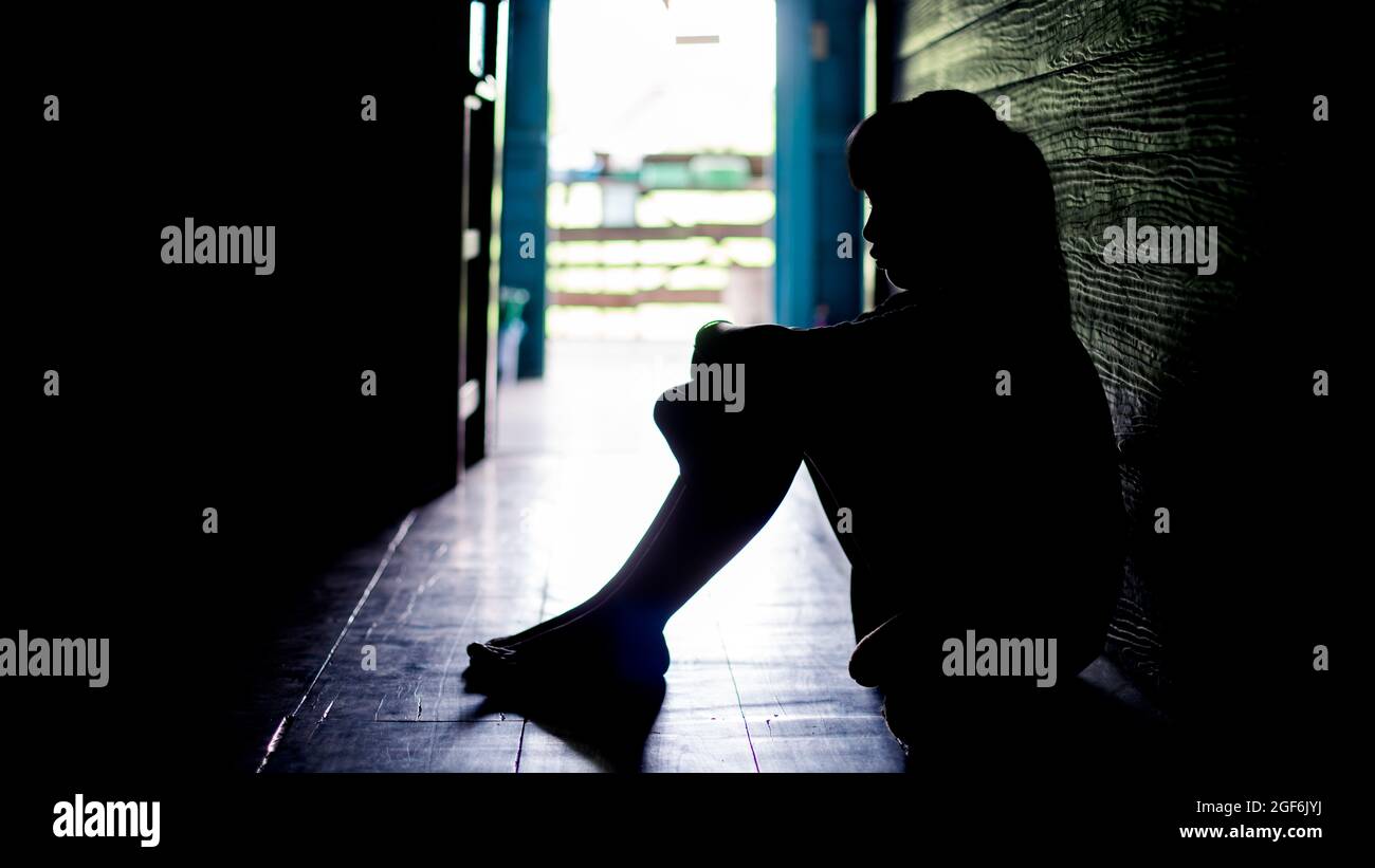 Triste petite fille solitaire pleurant en s'asseyant sur le sol dans la pièce sombre avec une ...