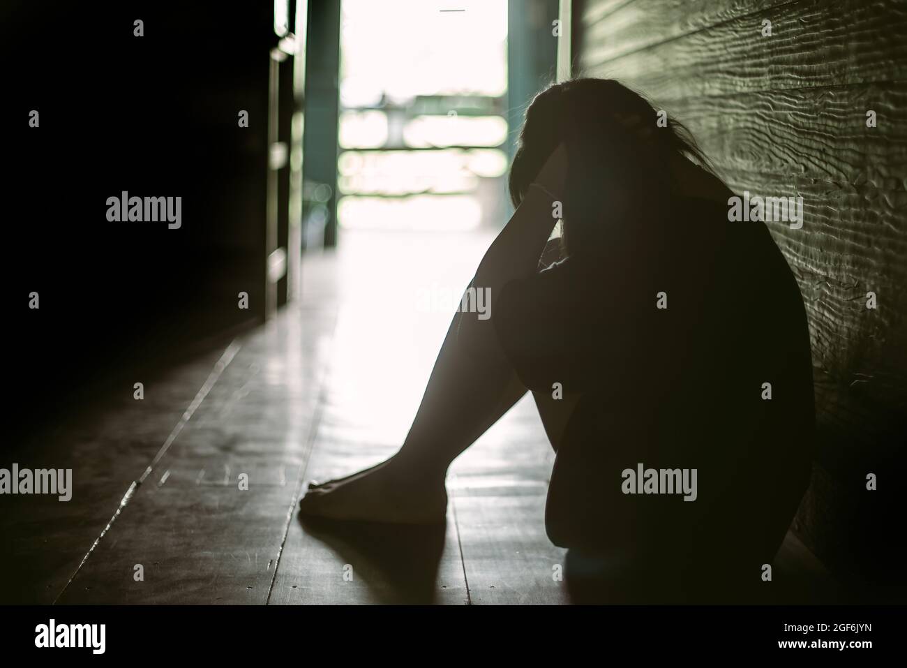 Triste petite fille solitaire pleurant en s'asseyant sur le sol dans la pièce sombre avec une ...
