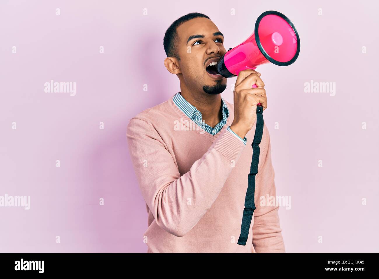 Un jeune homme afro-américain crie au mégaphone sur fond rose isolé ...