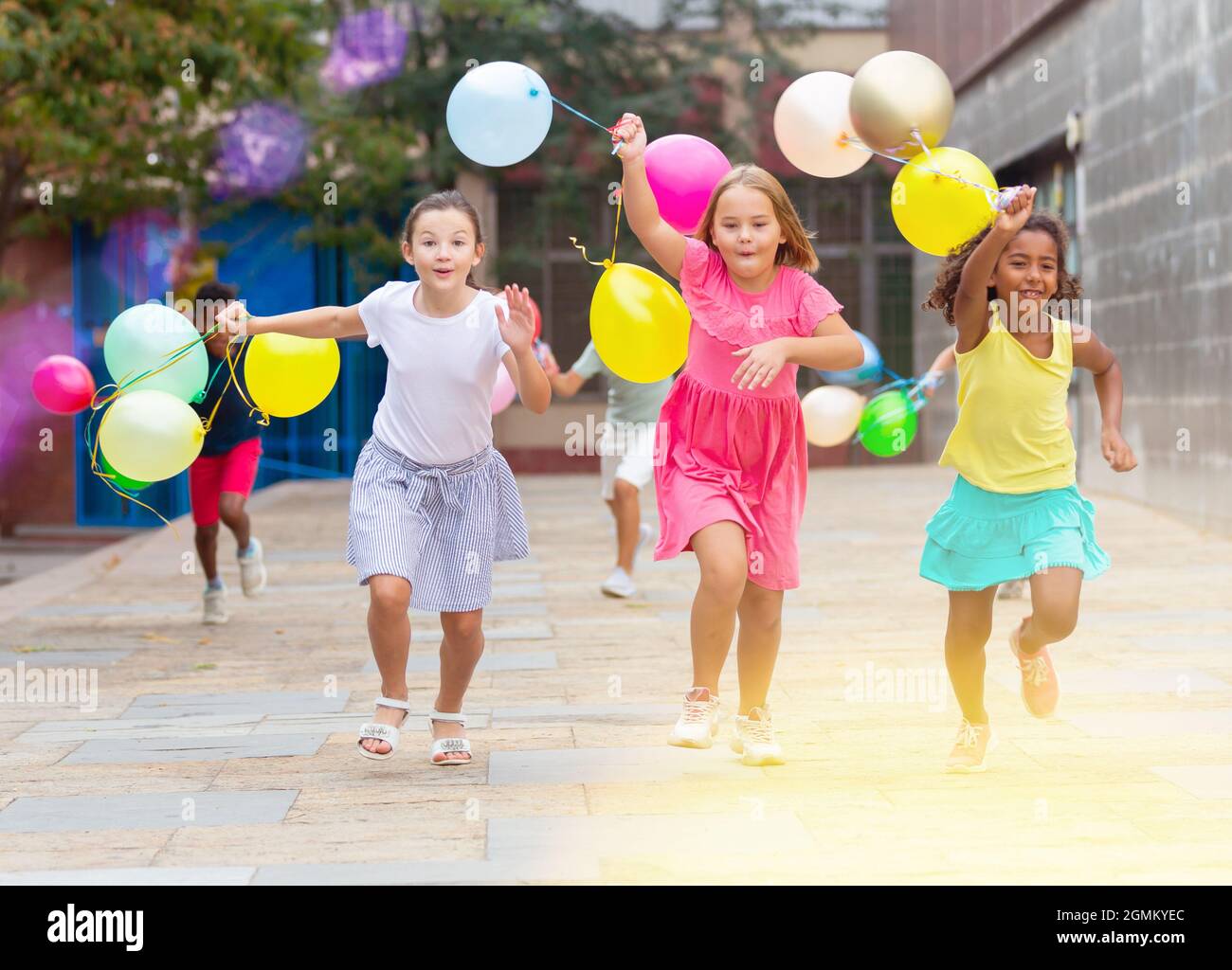 Les tweens heureux ont des ballons colorés qui se chassent les uns les autres dans la rue de la ...