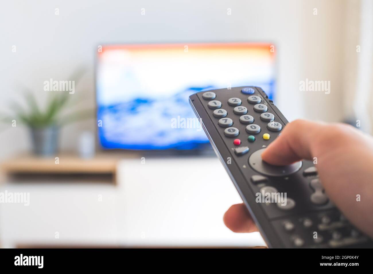 Tenez la télécommande du téléviseur dans la main, au premier plan, et ...