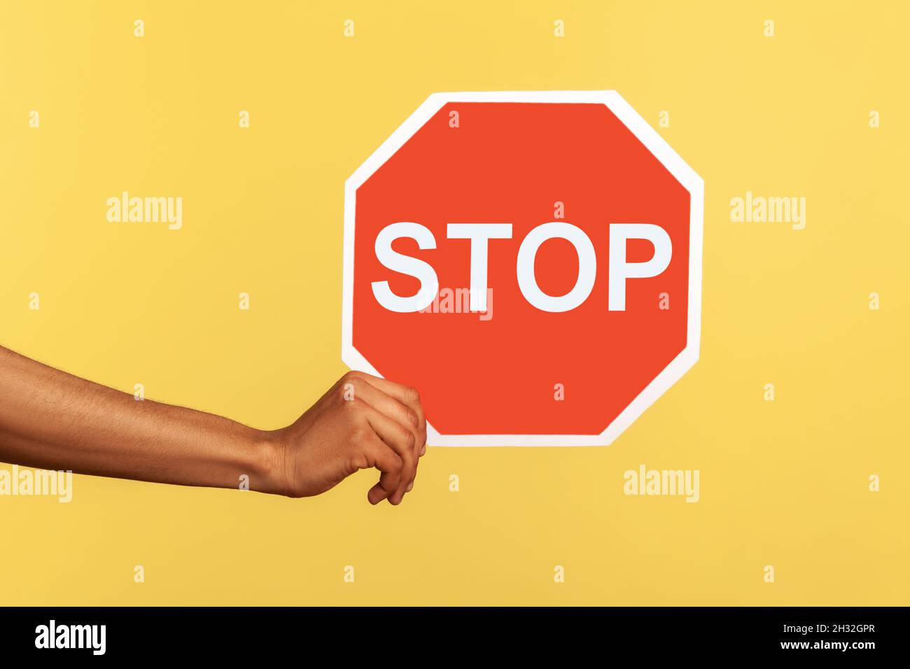 Gros plan d'une main mâle tenant un symbole d'arrêt octogonal rouge ...
