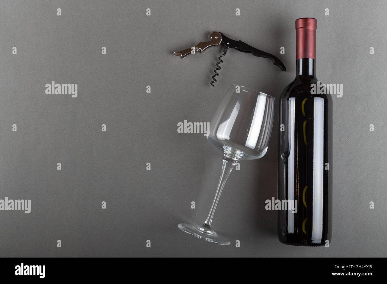 Bouteille de vin rouge, tire-bouchon et verre à vin vide sur fond gris ...