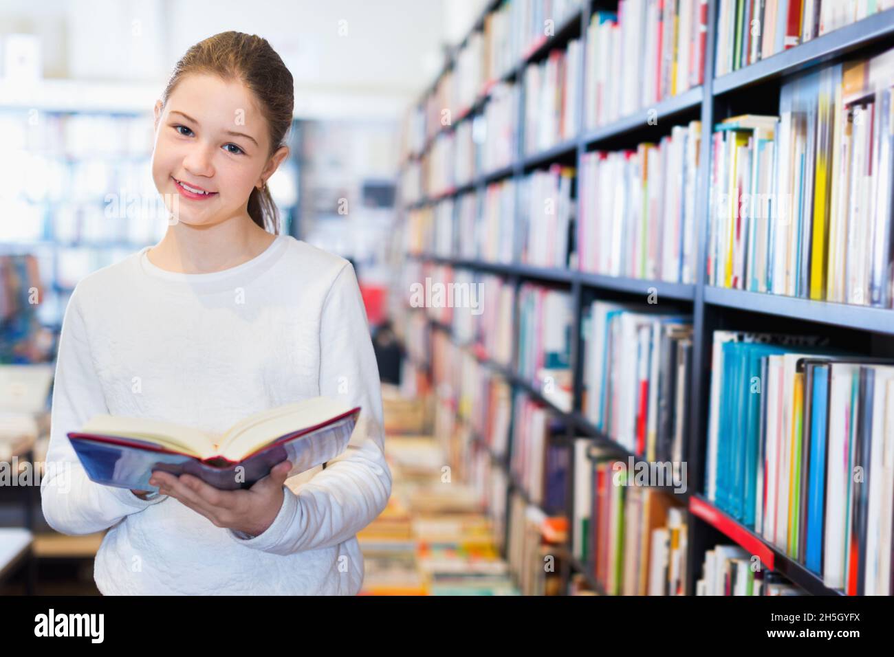 Une jeune fille intelligente debout seule près d'une bibliothèque dans ...