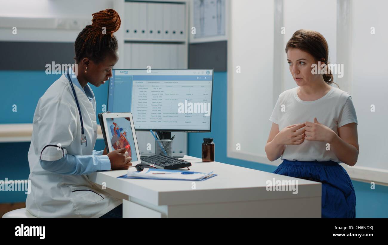 Médecin pointant vers une figure de cardiologie sur une tablette numérique pour expliquer le ...