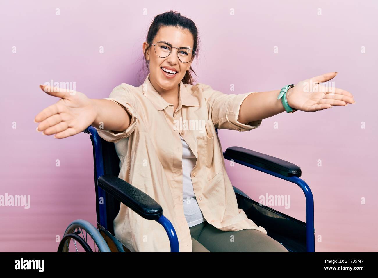 Jeune femme hispanique assise sur un fauteuil roulant regardant la ... Jeune femme hispanique assise sur un fauteuil roulant regardant la ...