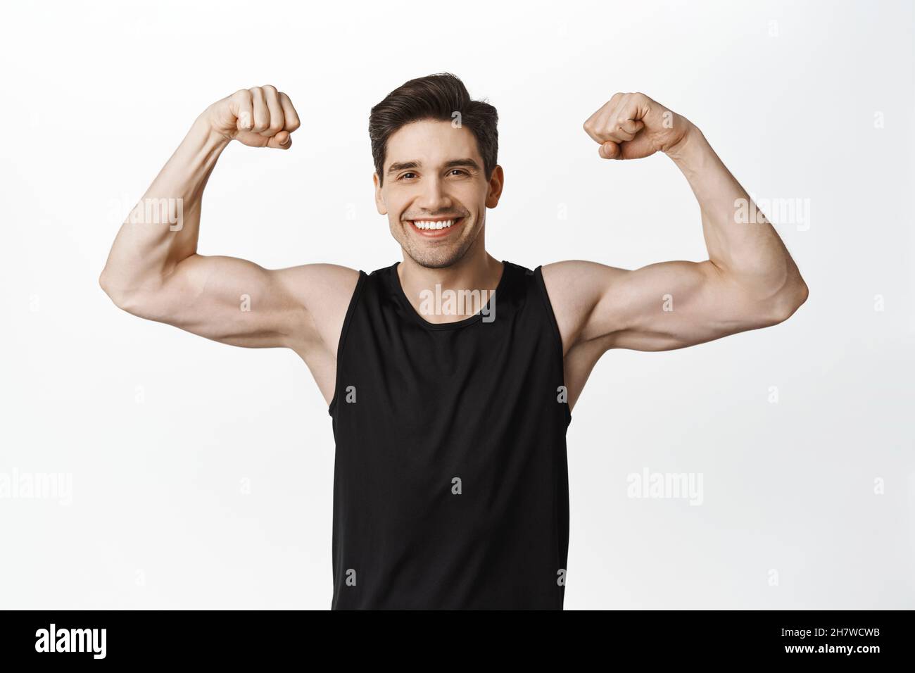 Sport et gym.Souriant jeune homme en bonne santé fléchissant biceps ...