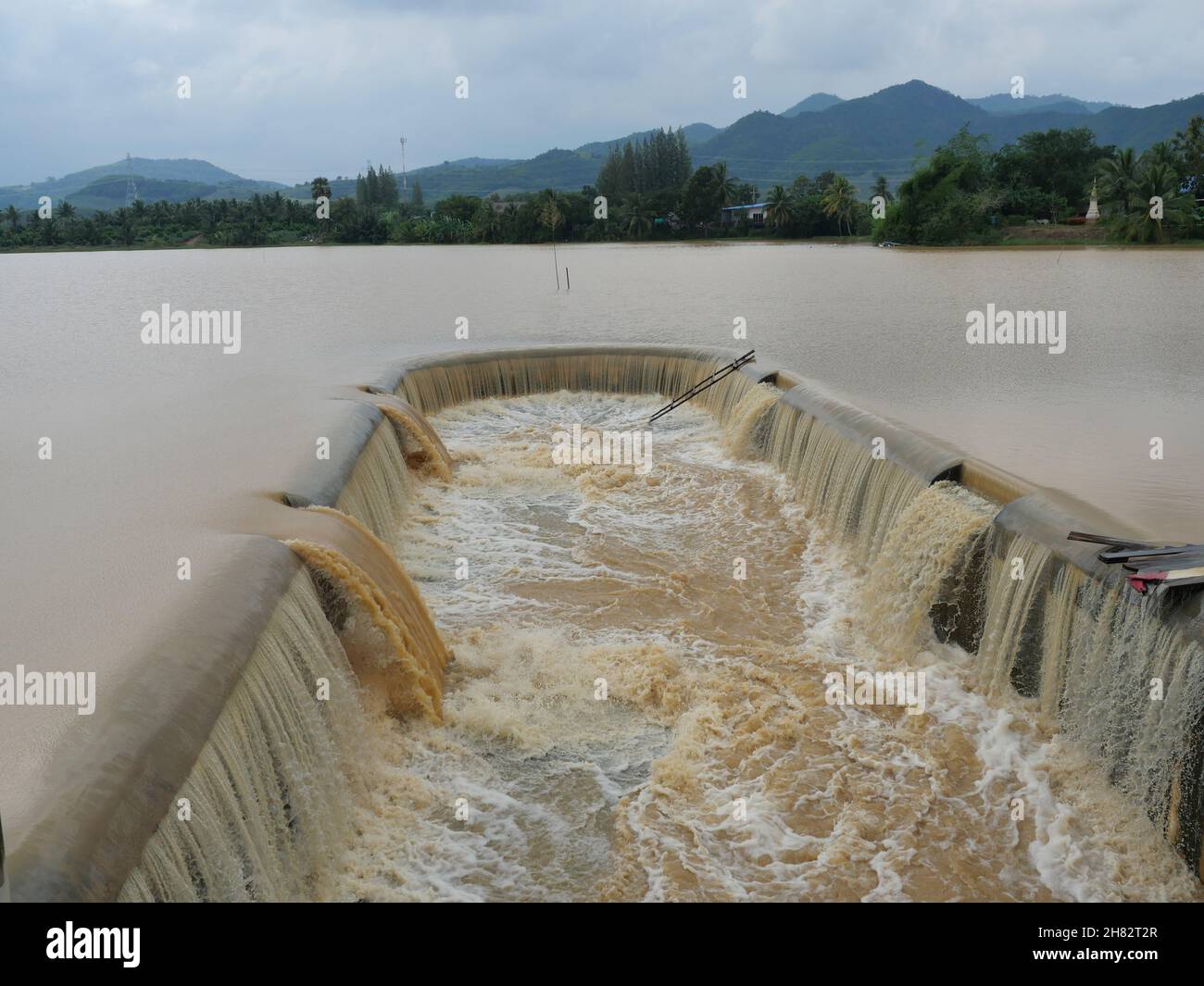 L'eau brune dans le barrage déborde dans le déversoir avec la montagne ...