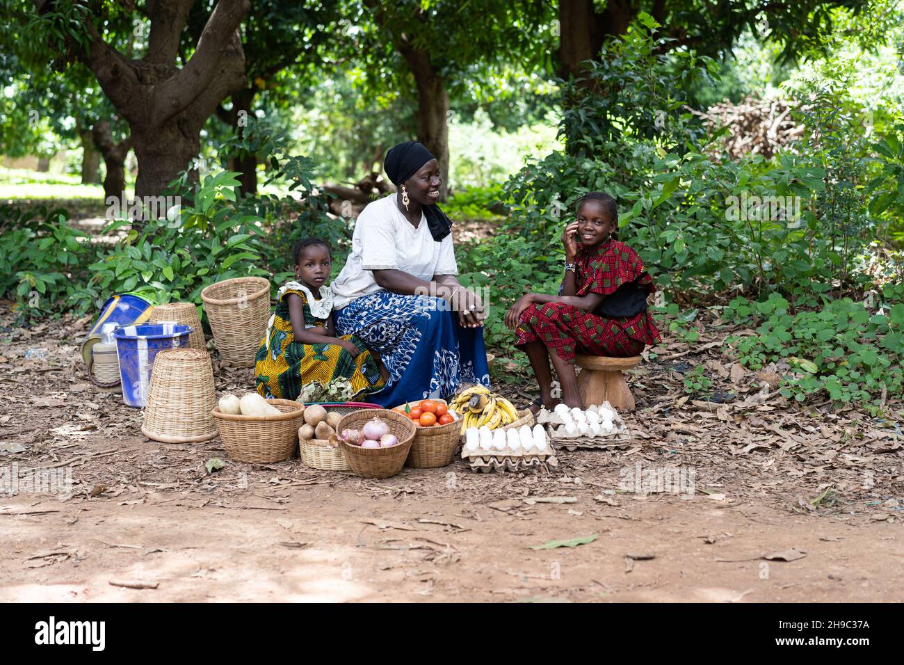 Un grand épicier noir africain souriant, assis avec ses deux filles à ...