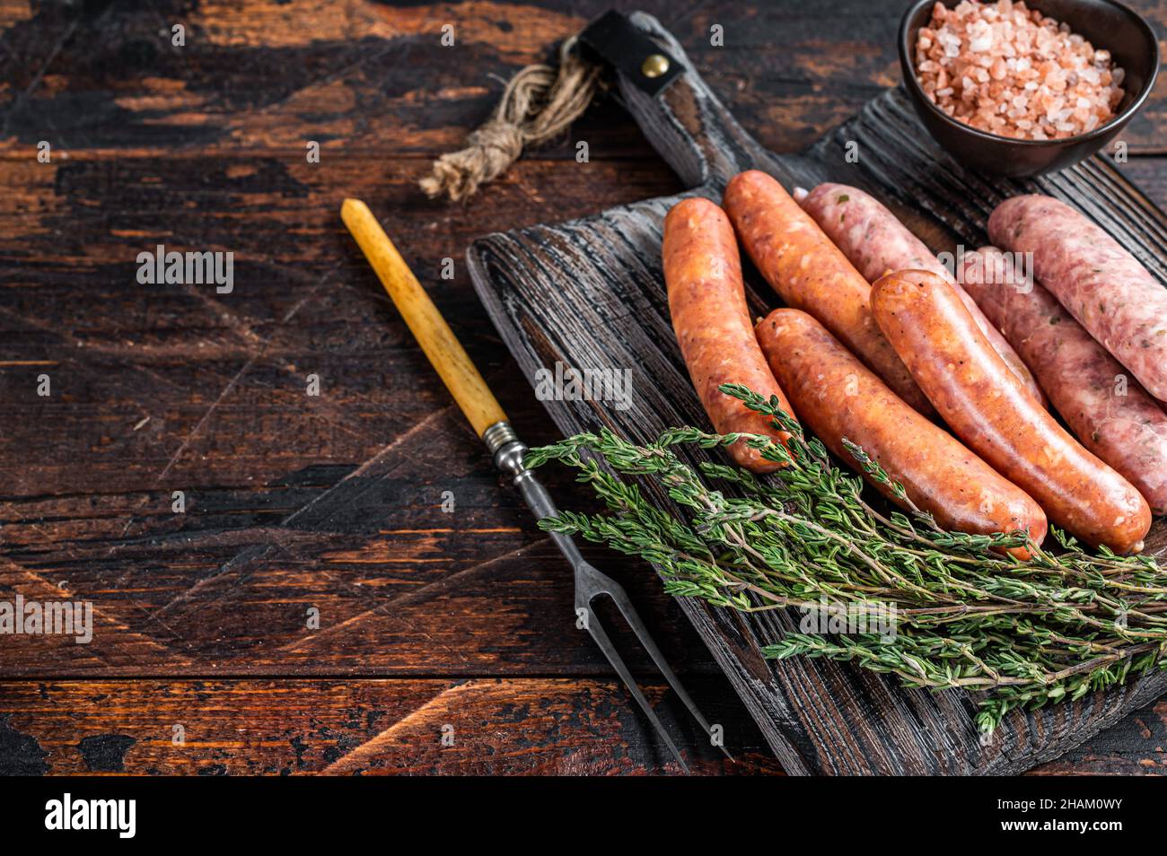 Assortiment de saucisses de porc et de bœuf crues aux épices sur une planche de bois au thym ...