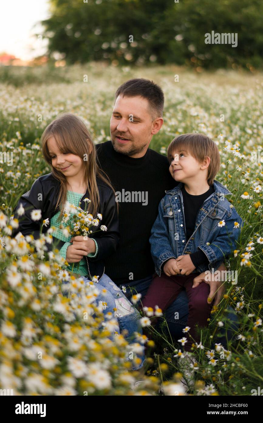 Père Avec Son Fils Et Sa Fille Accroupi Par Des Fleurs Dans Un Pré