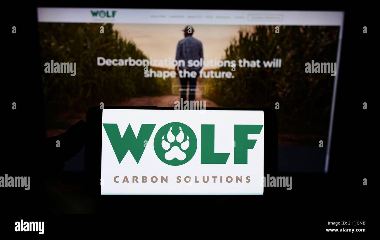 Personne tenant un smartphone avec le logo de la société Wolf Carbon Solutions à l'écran devant ...