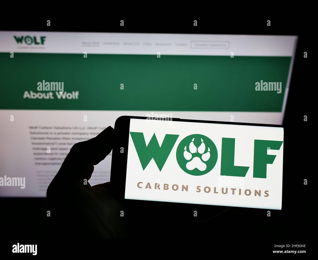 Personne tenant un téléphone mobile avec le logo de la société Wolf Carbon Solutions sur l'écran ...