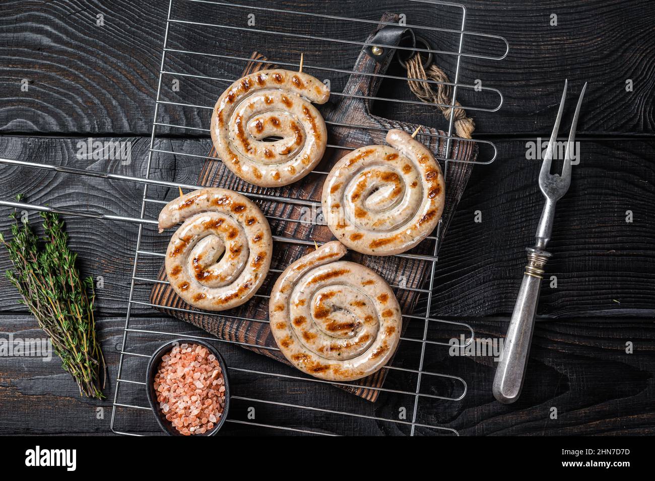 Barbecue de saucisses de viande de porc en spirale grillées sur un grill. Arrière-plan noir. Vue ...