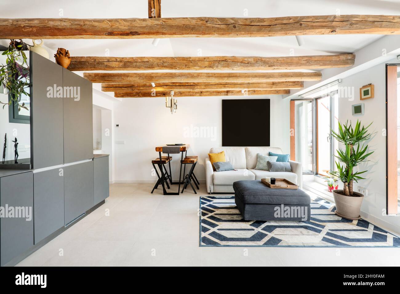 Séjour avec buffets gris, sortie sur une terrasse, canapés et poutres ...