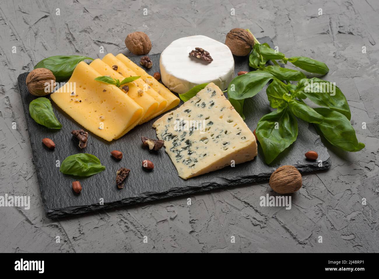 Différents types de fromages sur un tableau noir. Avec noix et basilic ...