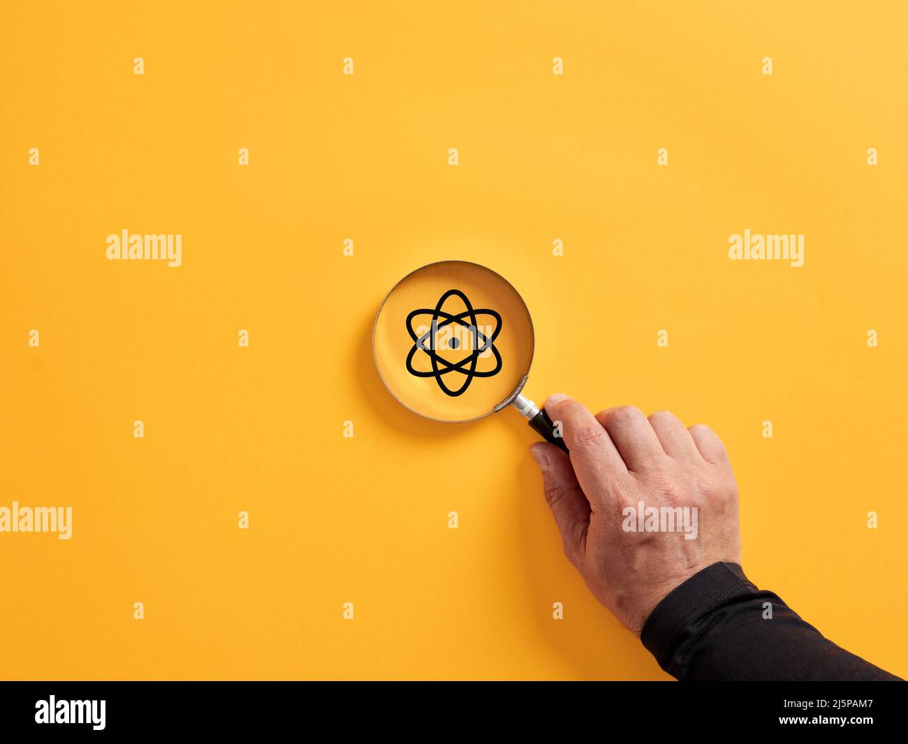 Main tenant une loupe sur le symbole de l'atome. Concept de la science ...
