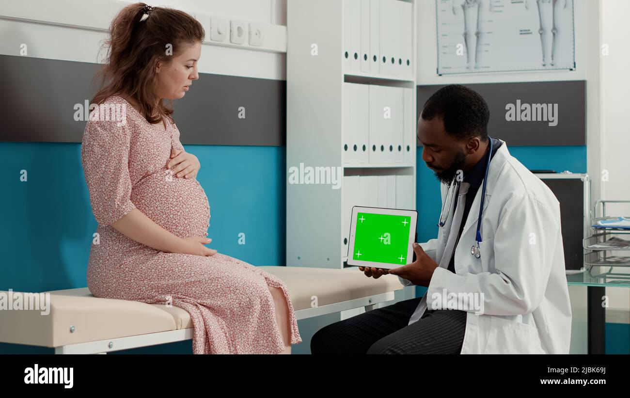 Patiente enceinte et médecin analysant un écran de santé horizontal sur une tablette numérique ...