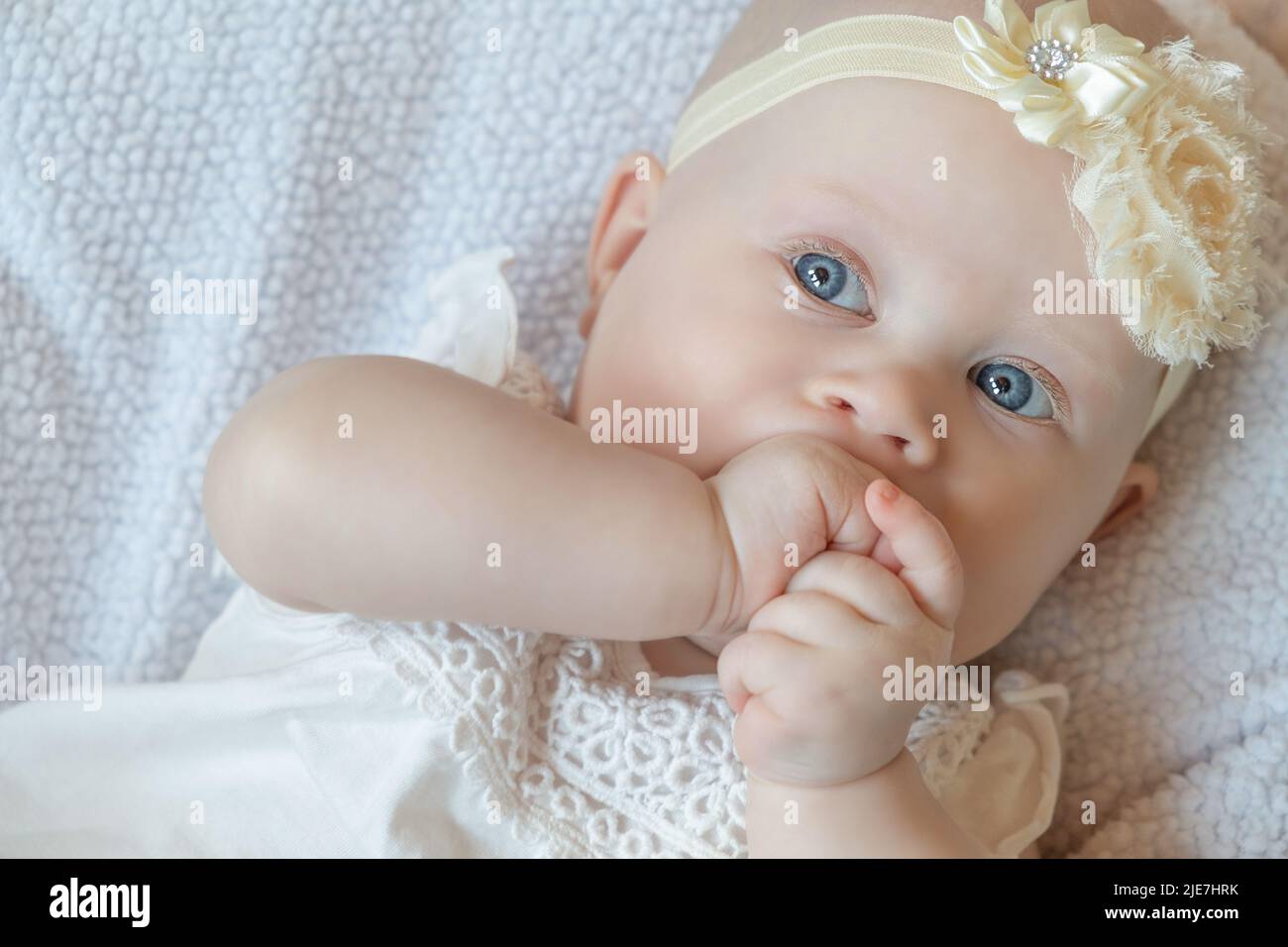 Bébé fille avec les yeux bleus suce son poing ou le doigt avec les ...