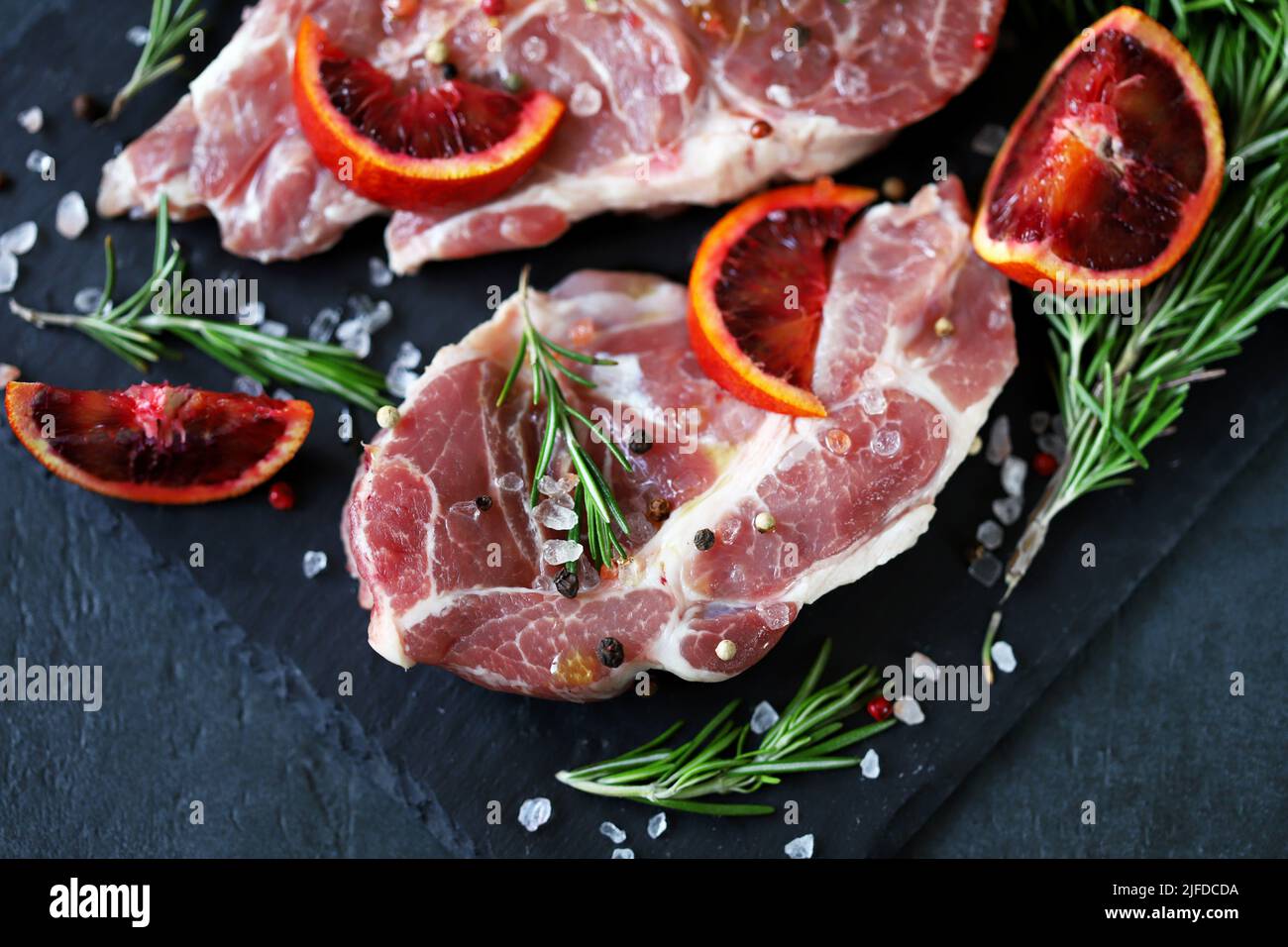 Steaks de porc crus marinés au romarin et à l'orange sur un panneau de ...