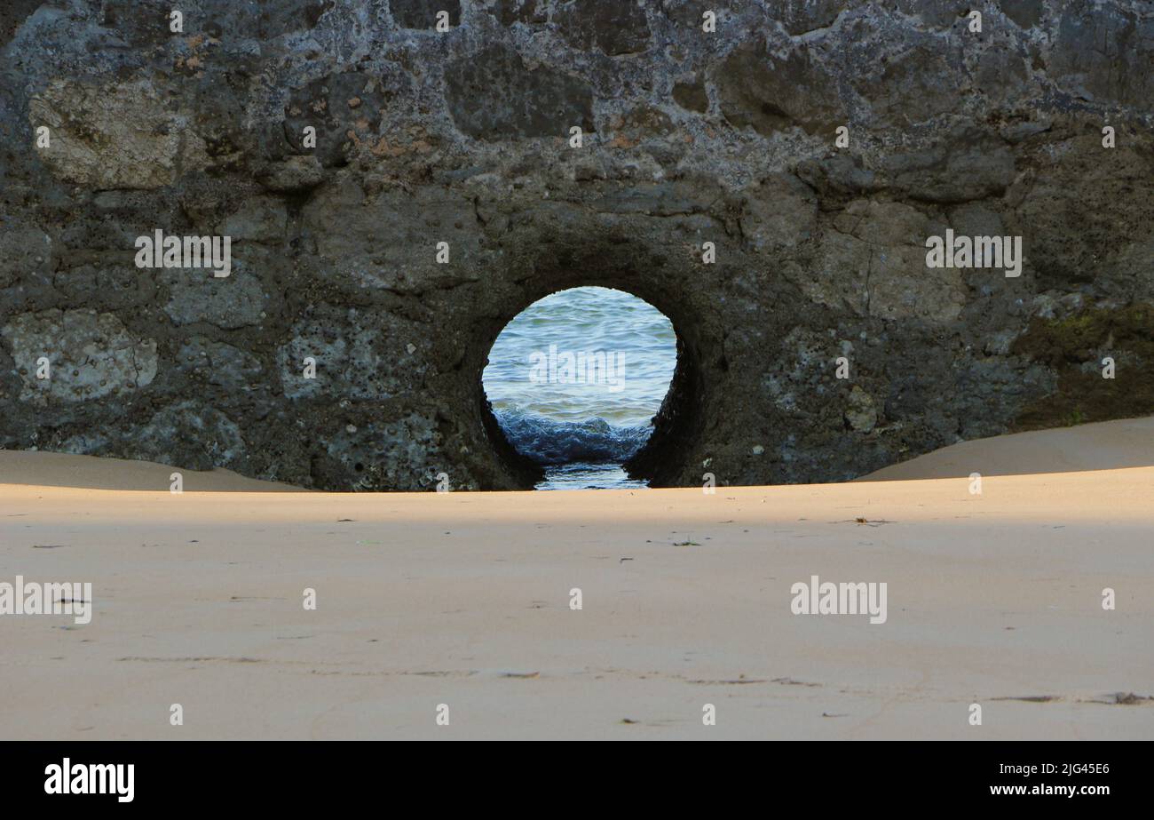 Vue sur la plage à travers une arche sur une jetée en pierre avec une ...