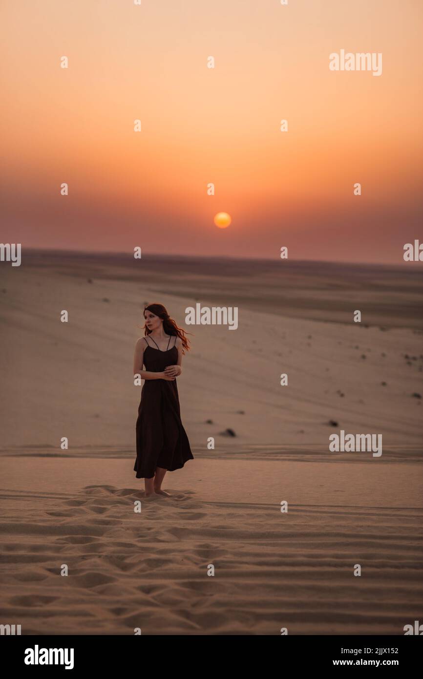 Femme en robe noire se promenant sur le sable tout en passant du temps ...