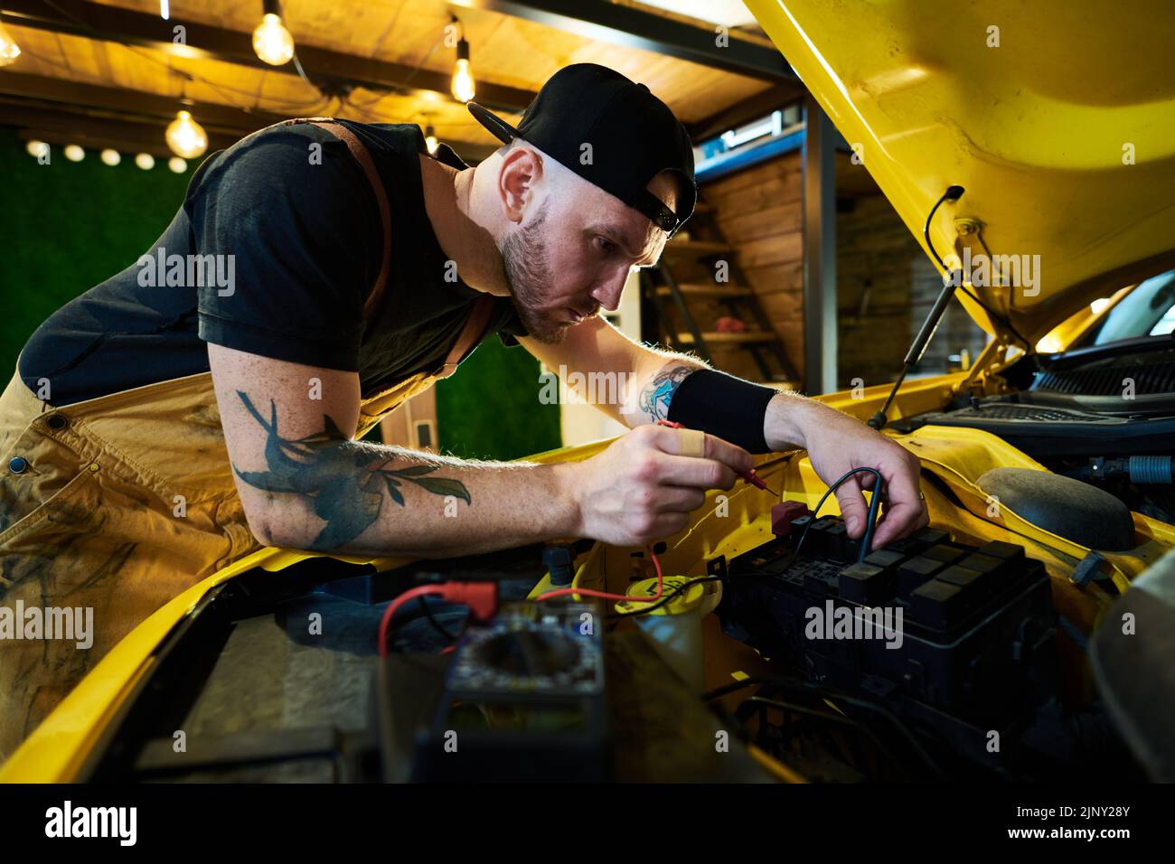 Jeune réparateur se repliant sur le capot ouvert avec le moteur pendant ...