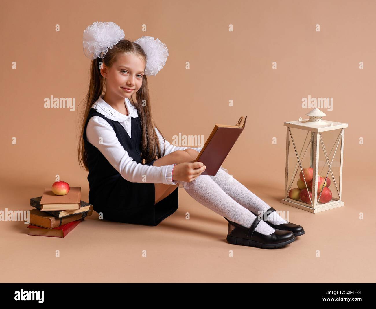 Une jeune fille dans un uniforme d'école assise sur le sol et tenant un livre Photo Stock - Alamy