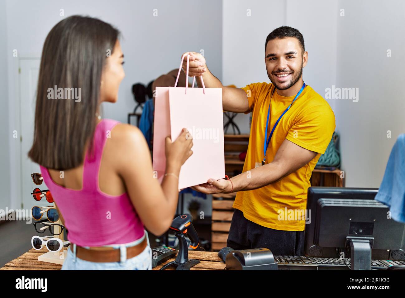 Jeune commerçant latin souriant heureux de donner son sac d'achats au ...
