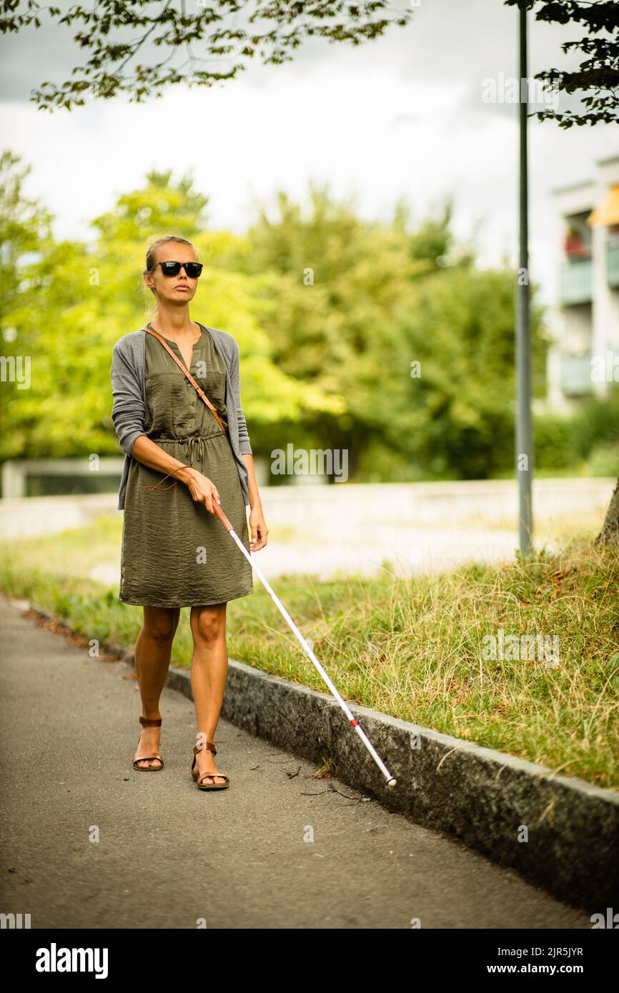 Femme aveugle marchant dans les rues de la ville, utilisant sa canne ...