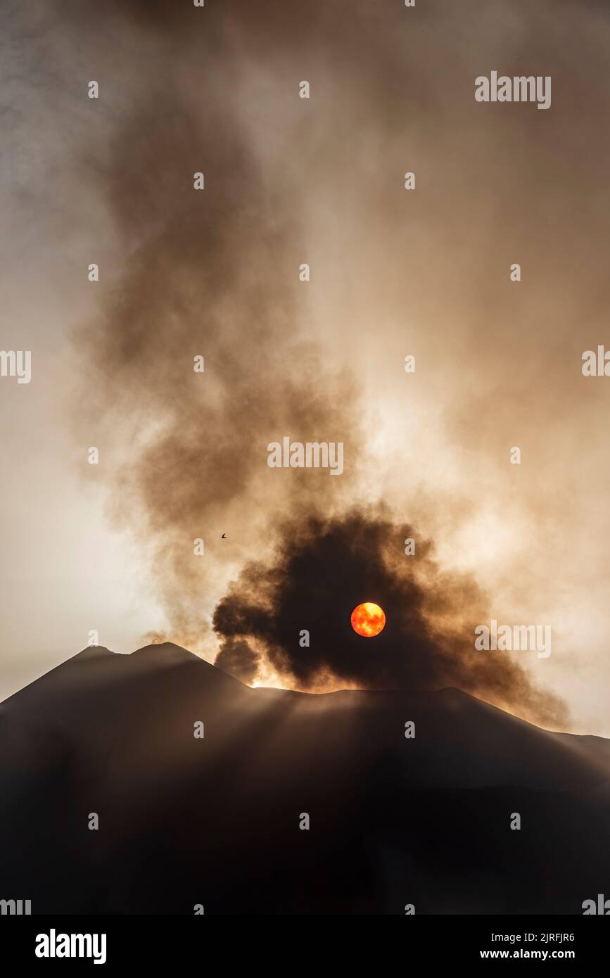 Le soleil couchant à travers un nuage de fumée et de cendres volcaniques qui coule des cratères ...