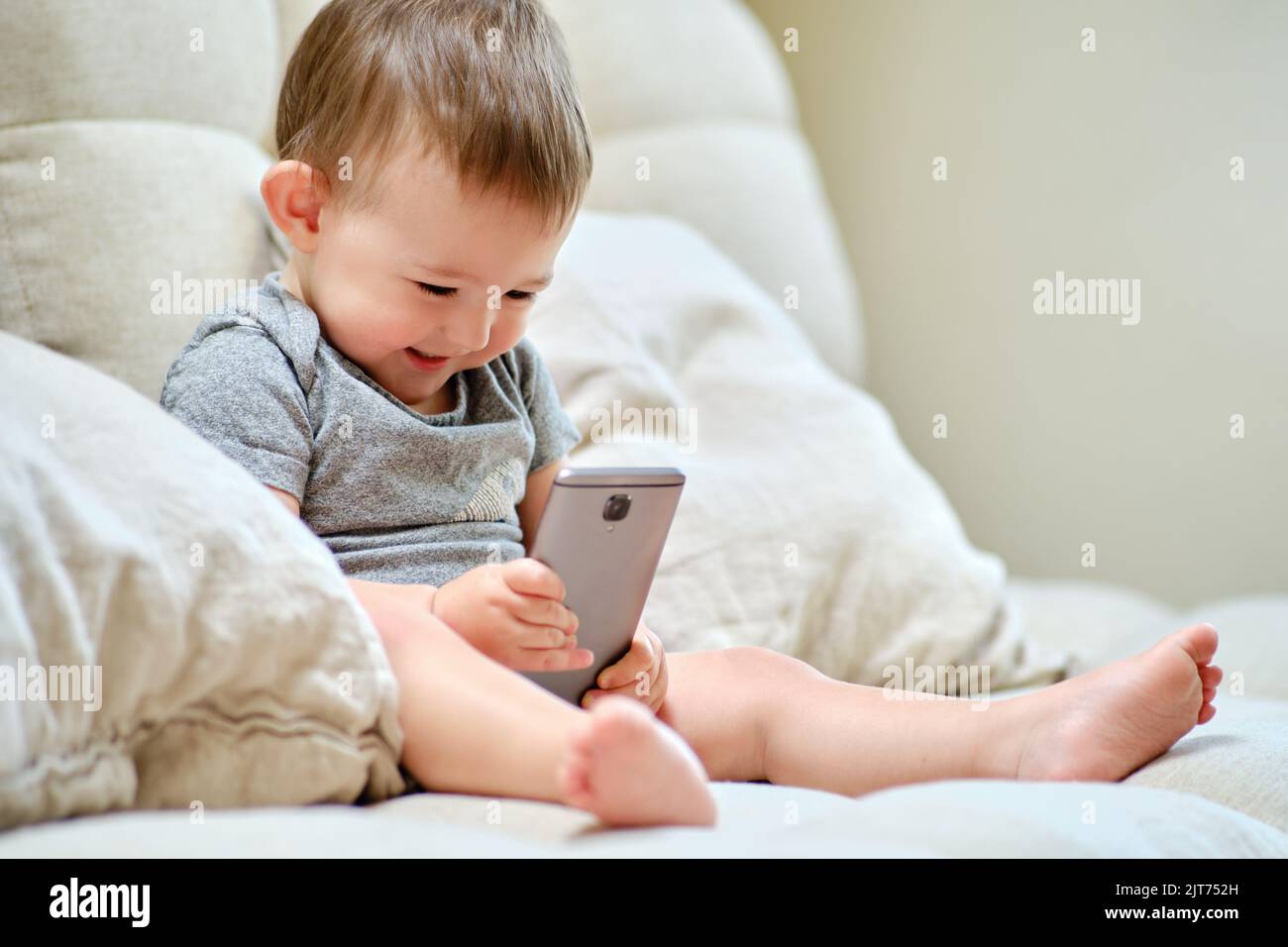 Bébé garçon heureux est assis avec un téléphone sur le canapé dans le ...