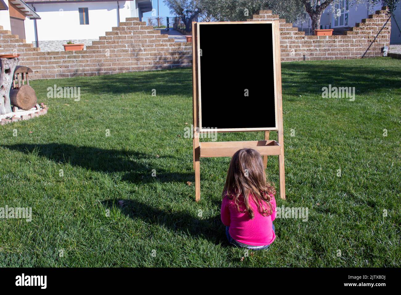 adorable petite fille assise dans le jardin regardant un tableau noir ...
