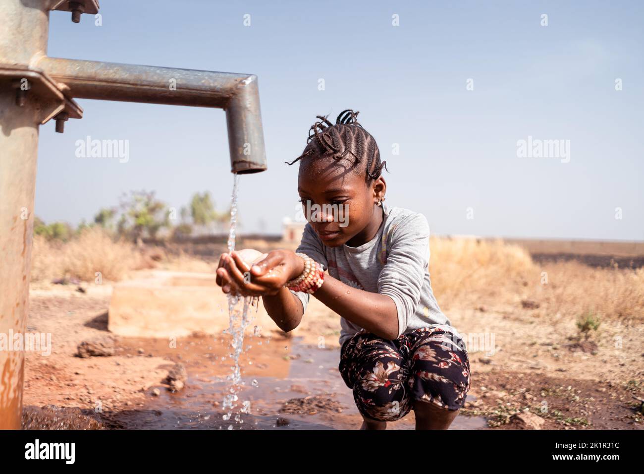 Smart petite fille africaine s'agenouillant devant un robinet de ...