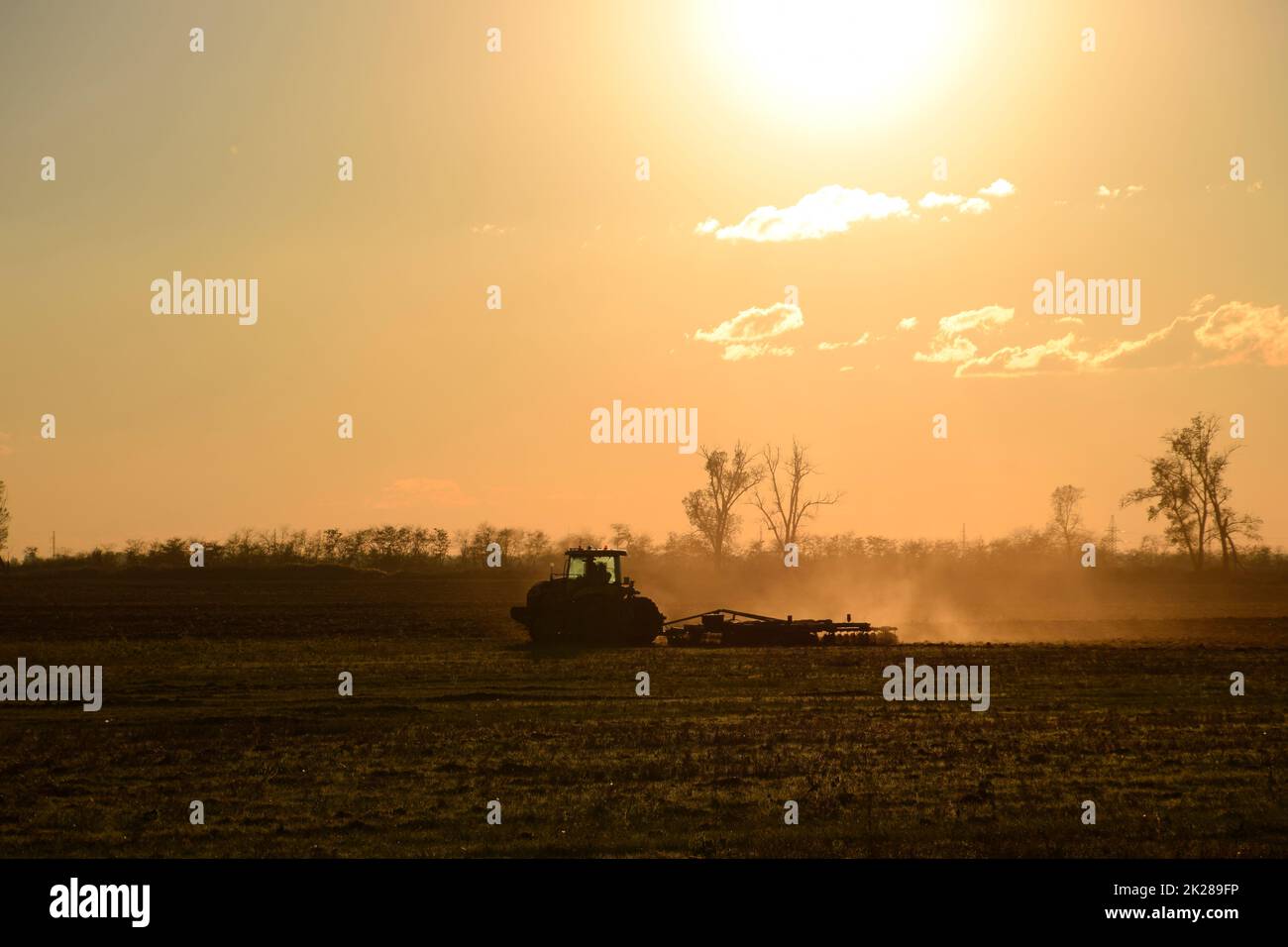 Tracteur au coucher du soleil labourer un champ. Labourage du sol à l ...