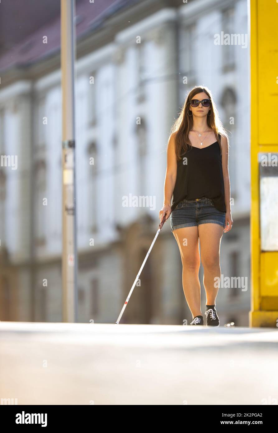 Femme aveugle marchant dans les rues de la ville, utilisant sa canne ...