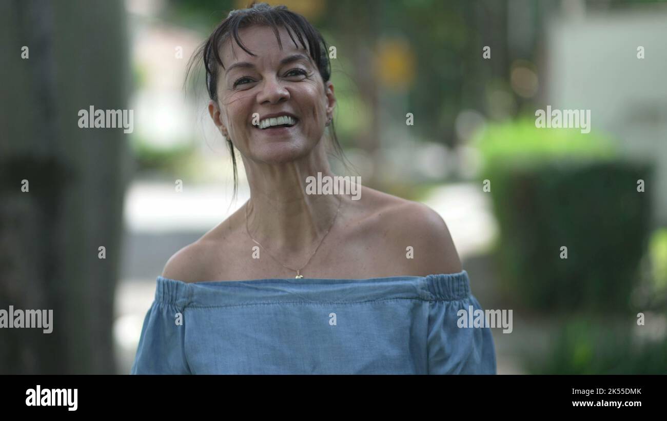 Une femme heureuse et âgée qui marche dans la rue souriant à l'appareil photo. Une femme de 50s ...