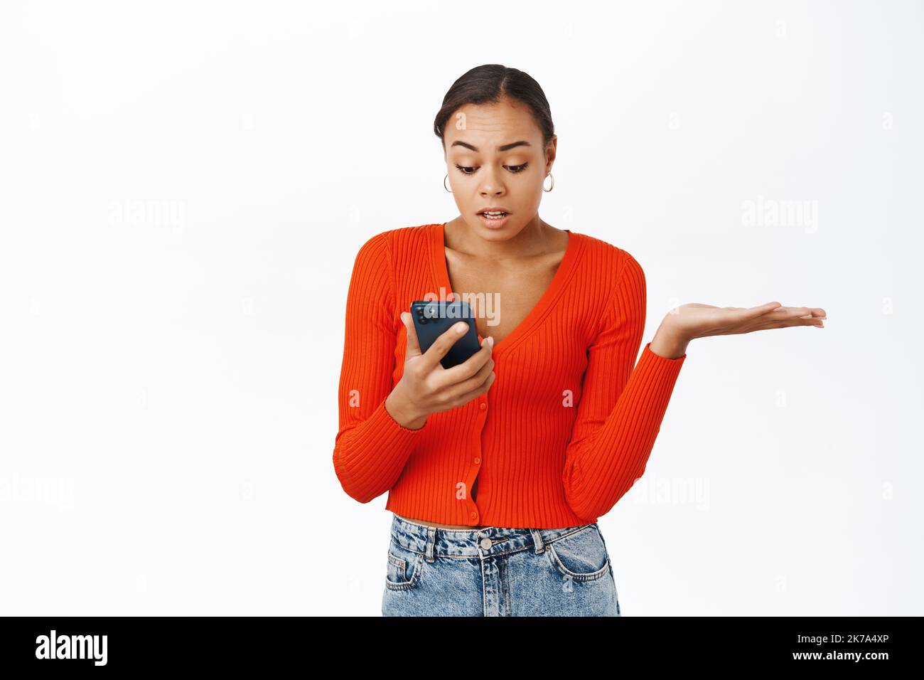 La femme semble confuse à l'écran du smartphone, hausse les épaules et ...