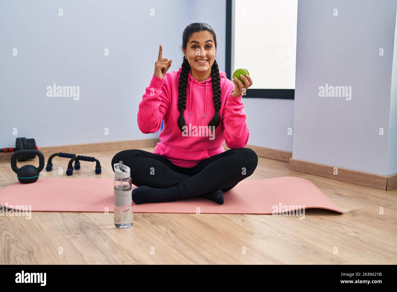 Jeune femme hispanique assise sur un tapis de yoga mangeant de la pomme ... Jeune femme hispanique assise sur un tapis de yoga mangeant de la pomme ...