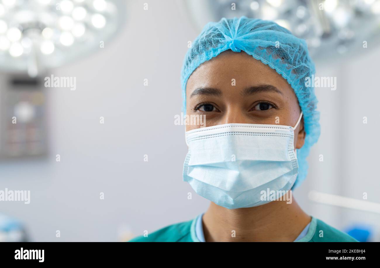 Portrait de la femme chirurgien biracial dans le masque chirurgical, le ...