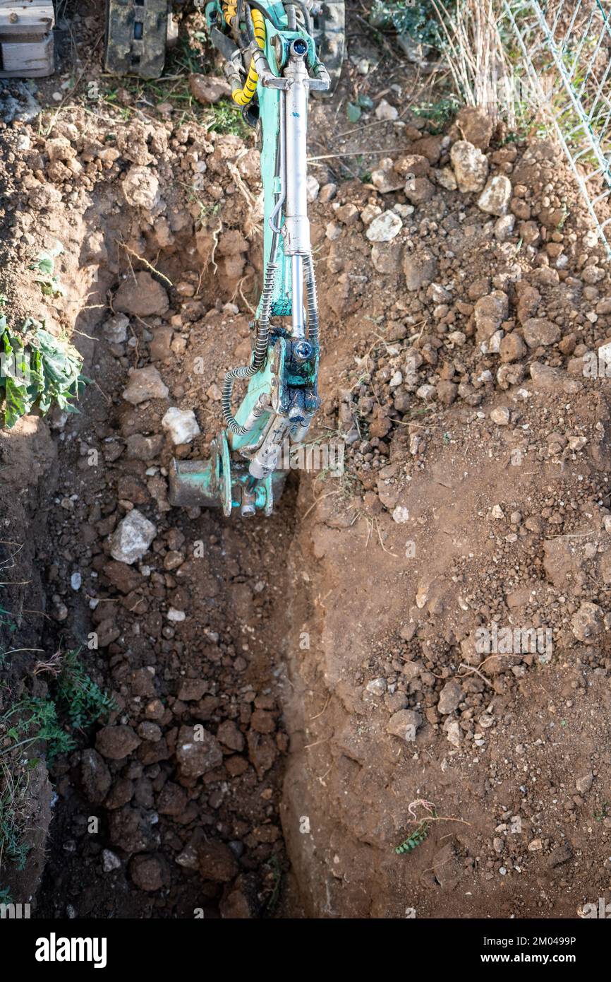 Une minipelle creuse une tranchée pour poser les tuyaux. Gros plan d ...