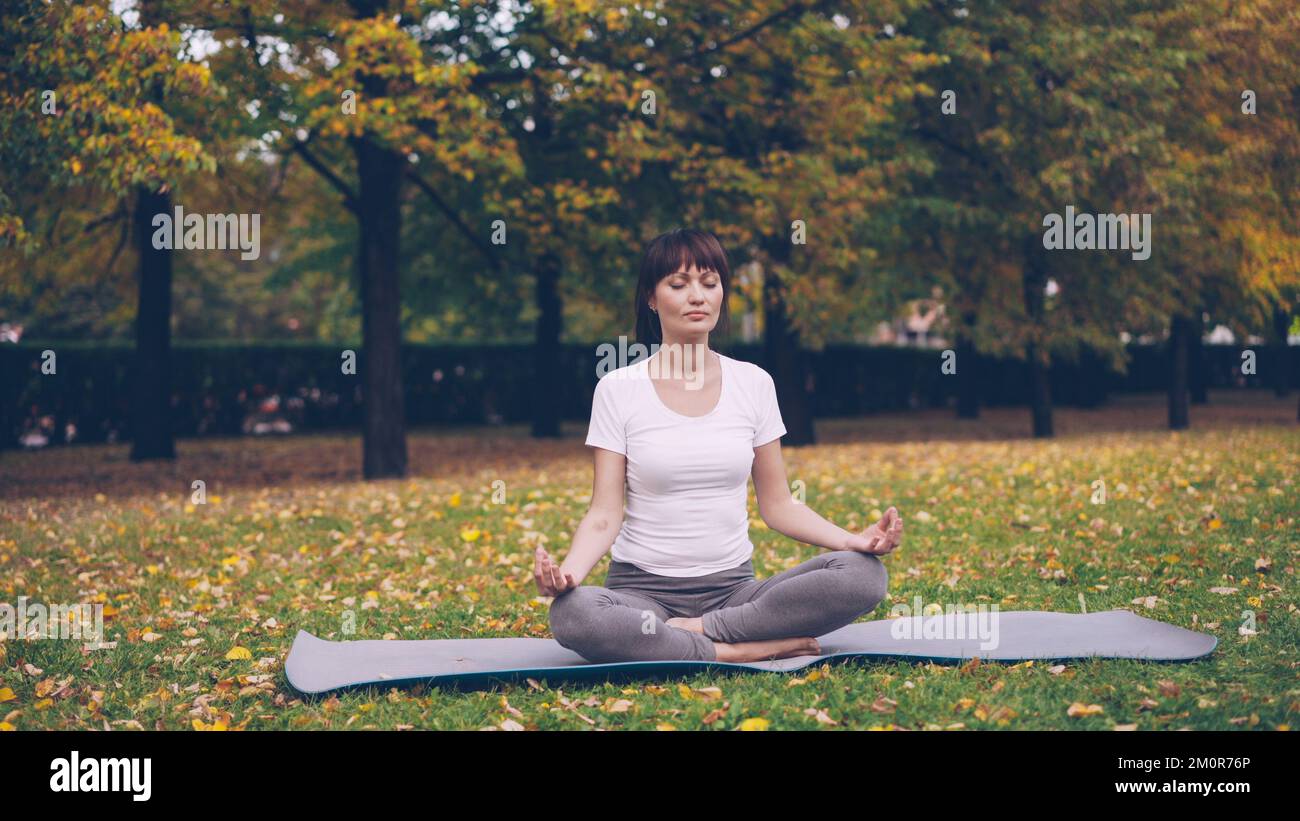 Belle jeune femme est assise en position lotus sur le tapis de yoga ...