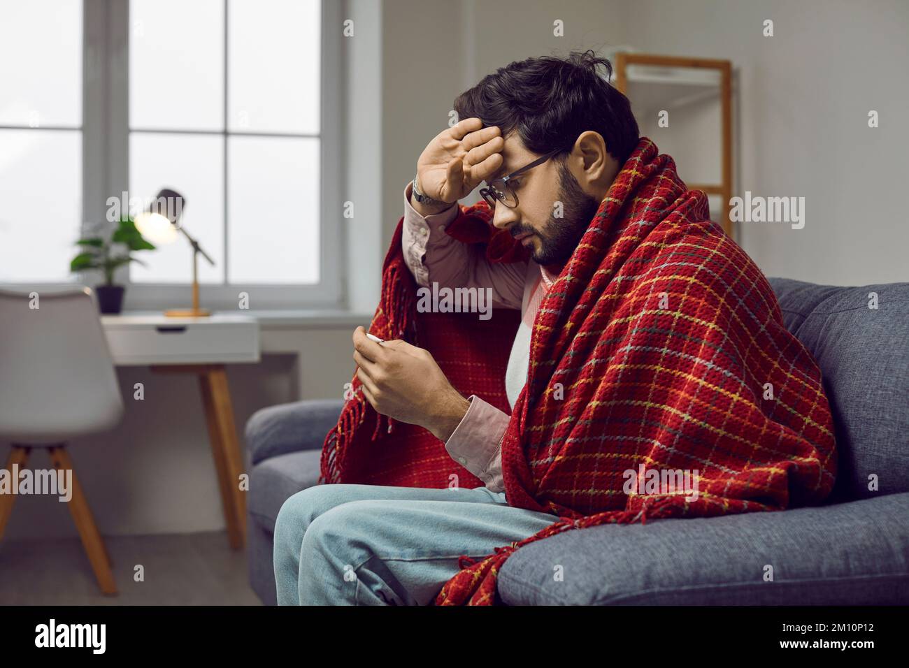 L'homme avec une fièvre mesure sa température, regarde le thermomètre ...