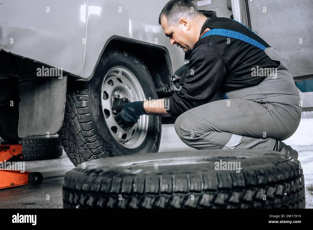 L'homme change la roue de la voiture dans le service de voiture. Un mécanicien automobile ...