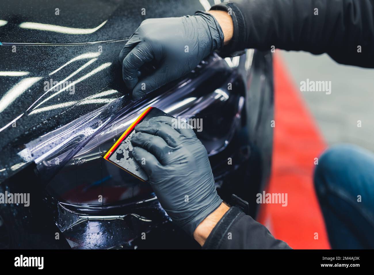 Gros plan d'une personne portant des gants noirs appliquant un film de protection de peinture ...