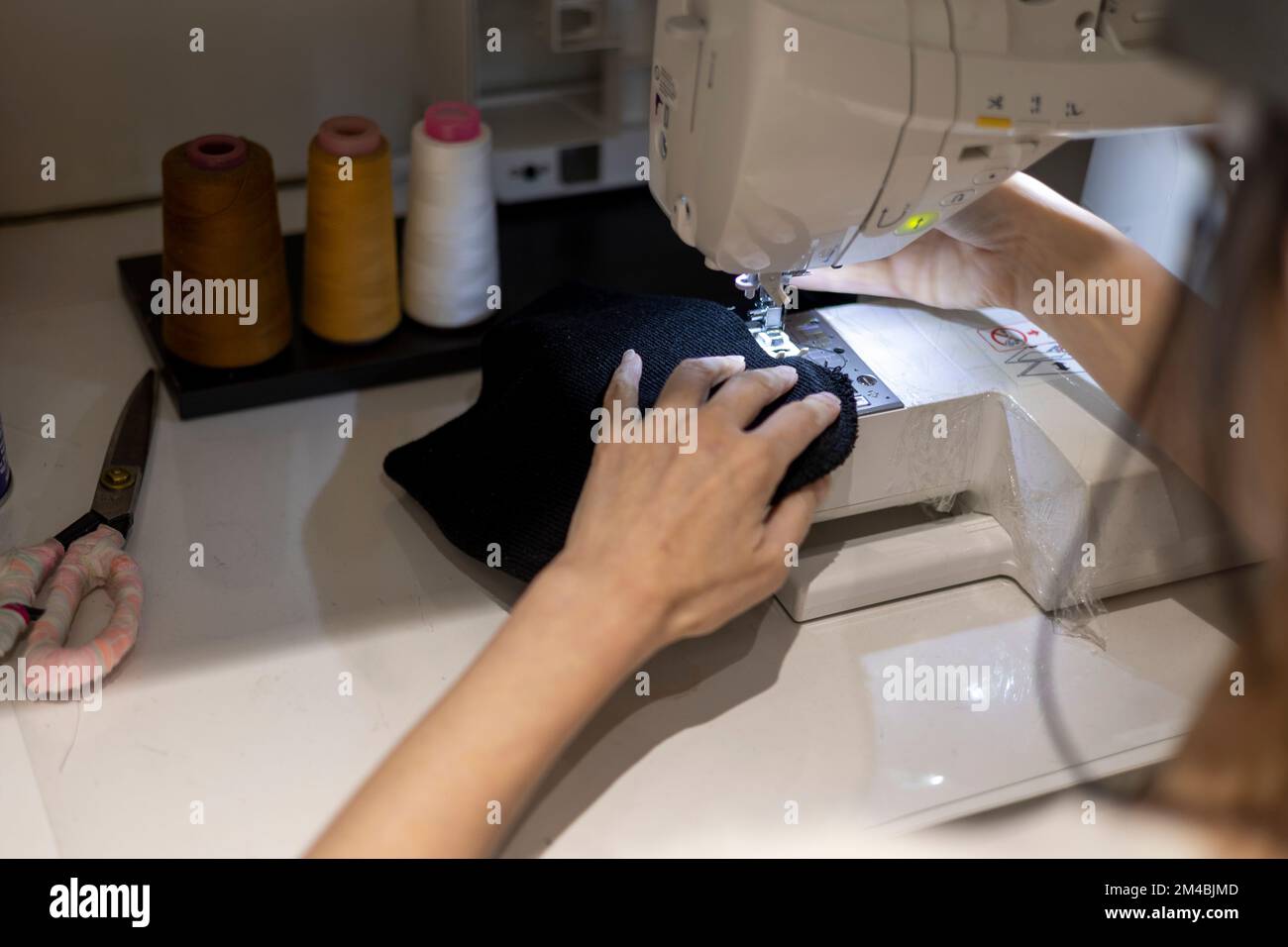 La femme est en train de coudre un bonnet beanie noir sur une machine à ...