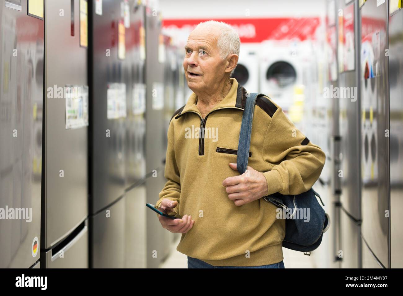 homme âgé qui choisit un réfrigérateur dans la salle d'exposition du ...