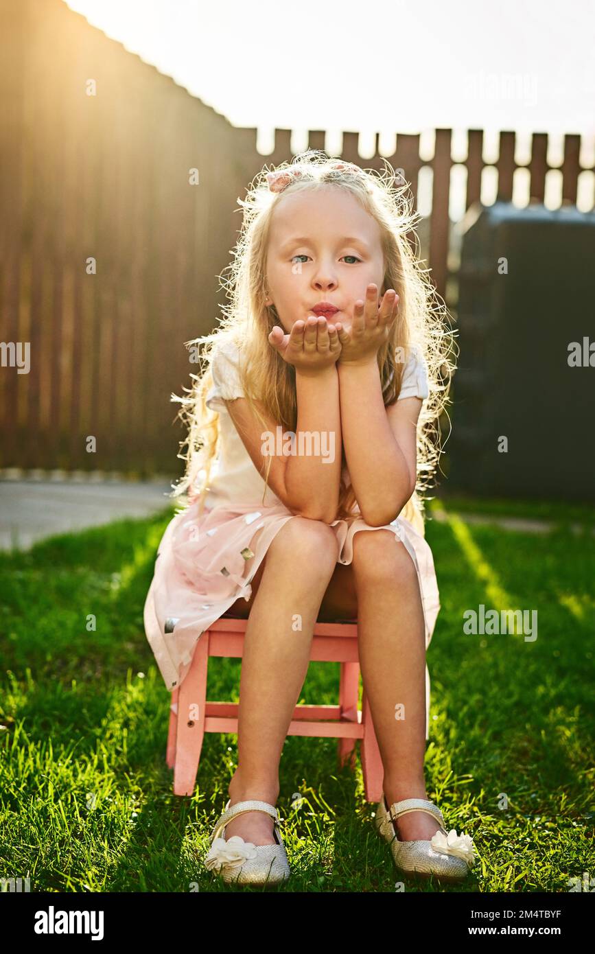 Je t'aime aussi maman. Portrait d'une petite fille gaie assise sur une chaise et souffle un ...